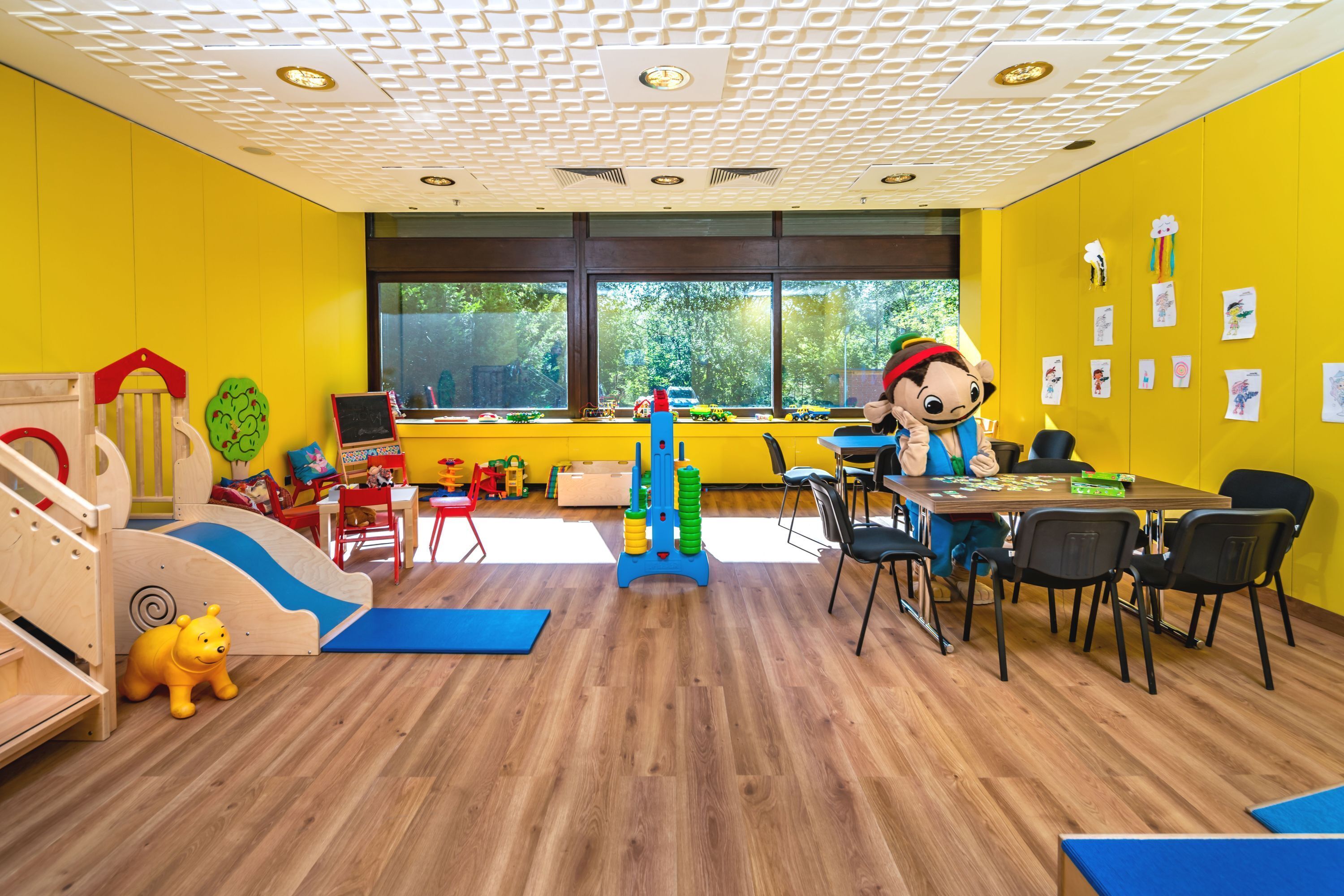 Uma sala de brinquedos infantil, vibrante, com um escorregador, espa ço para brincar e um brinquedo de pelúcia grande.