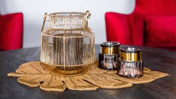 Um recipiente de vidro decorativo com alças, dois recipientes de vidro menores e um jogo de mesa tecido sobre uma mesa.