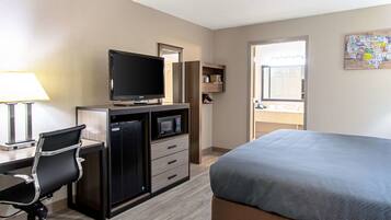 Quarto de hotel com cama, escrivaninha, cadeira, televisão, micro-ondas e um pequeno frigorífico.