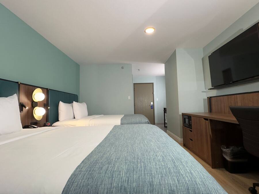 Quarto de hotel com uma cama grande, uma escrivaninha, uma televisão e uma porta.