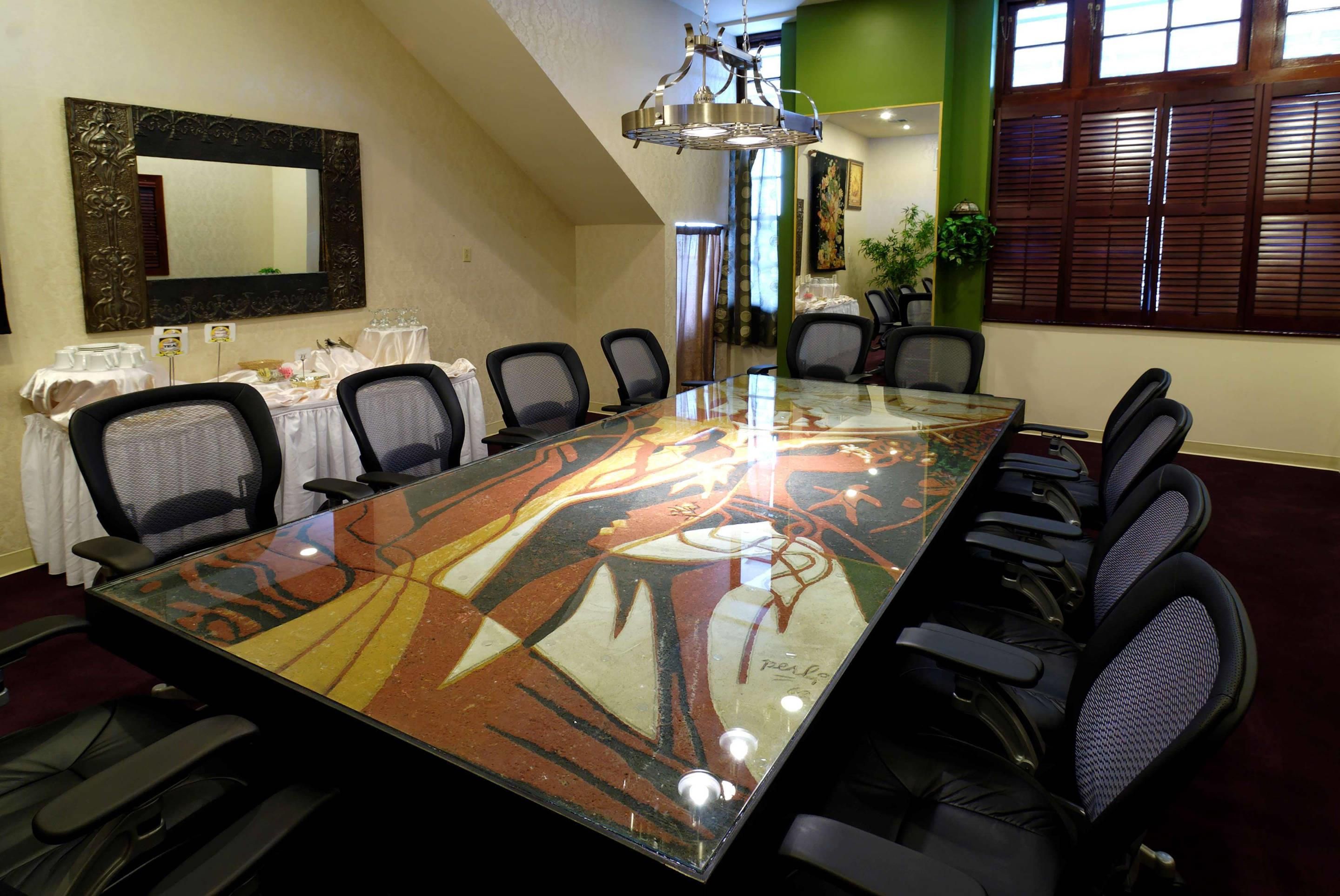 Uma sala de conferências com uma mesa comprida, várias cadeiras, um candelabro e um espelho grande na parede.