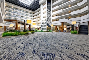 Um átrio de hotel em vários níveis, com um espaço aberto central, múltiplas varandas e plantas dentro de casa.