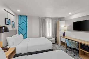 Quarto de hotel com duas camas, uma escrivaninha, televisão e uma janela com cortinas.