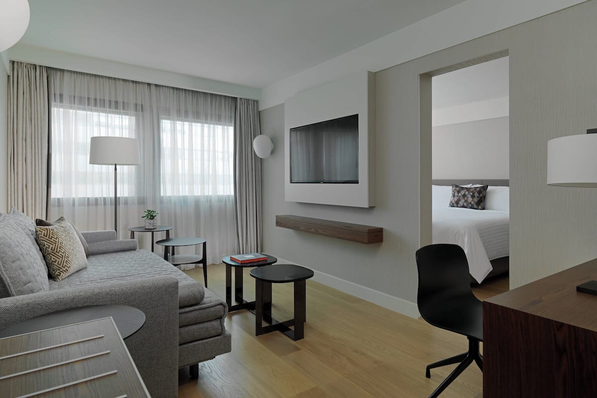 Quarto de hotel moderno com sofá, escrivaninha, cadeira, televisão e cama.