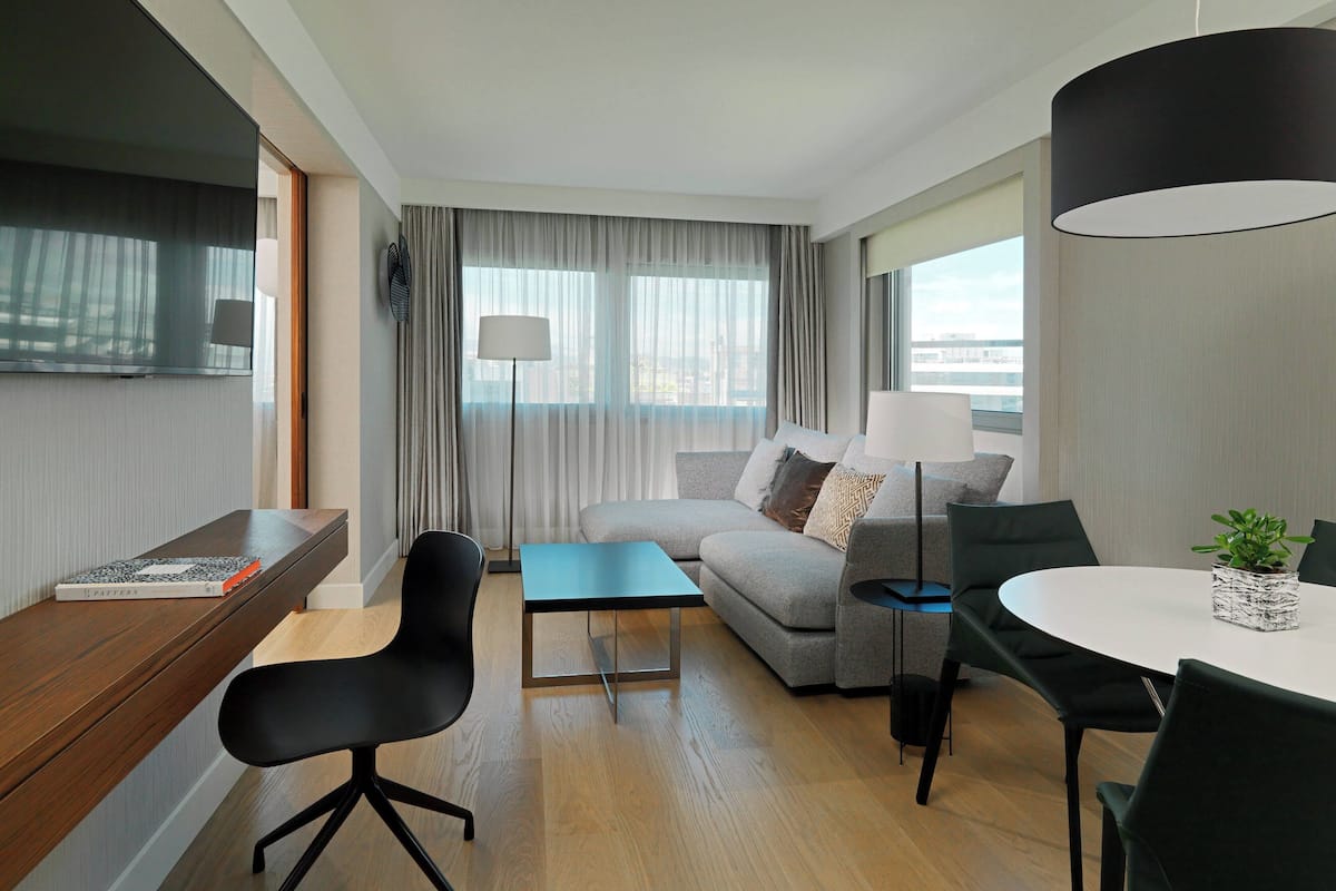 Quarto de hotel moderno com sofá, uma pequena mesa, escrivaninha e mesa de jantar.