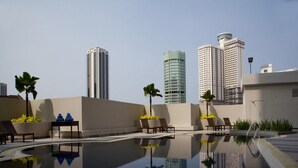 Piscina no terraço com espreguiçadeiras e palmeiras, cercada por edifícios altos.