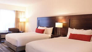 Quarto de hotel com duas camas, uma escrivaninha e uma cadeira.