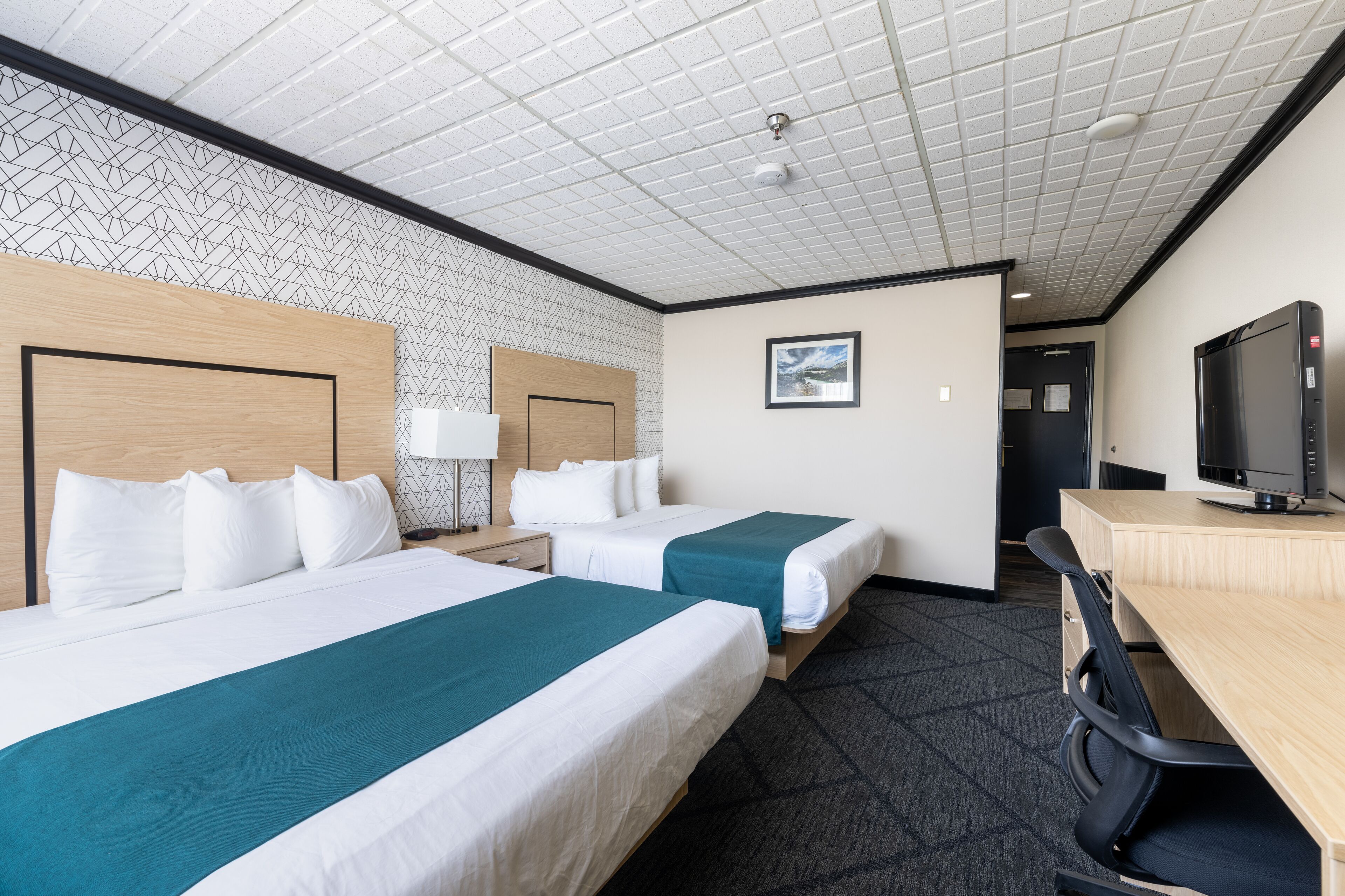 Quarto de hotel com duas camas, uma escrivaninha com computador e televisão.