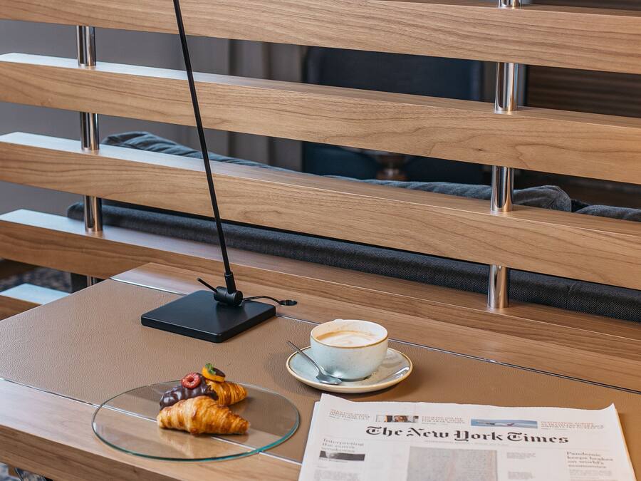 Um banco de madeira com um laptop, uma chávena de café, um croissant e um jornal.