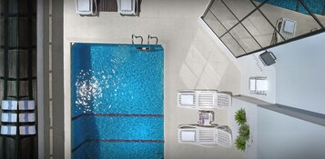 Vista aérea de um quarto de hotel com uma piscina grande, uma espreguiçadeira e uma pequena mesa com uma cadeira.