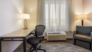 Quarto de hotel com escrivaninha, cadeira de escritório, duas luminárias, sofá e aparelho de ar condicionado.
