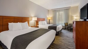 Quarto de hotel com duas camas, uma mesa de trabalho e uma televisão, e uma cadeira.