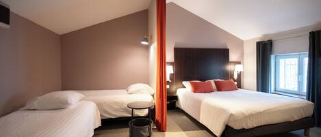 Quarto de hotel com duas camas de solteiro, uma cama grande, uma mesinha e uma cadeira.
