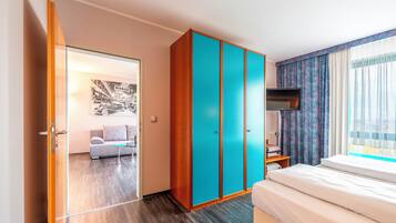 Quarto de hotel com cama, guarda-roupa, televisão e janela com cortinas.