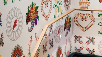 Uma escadaria com corrimão de madeira e parede decorada com diversos padrões florais e geométricos coloridos.