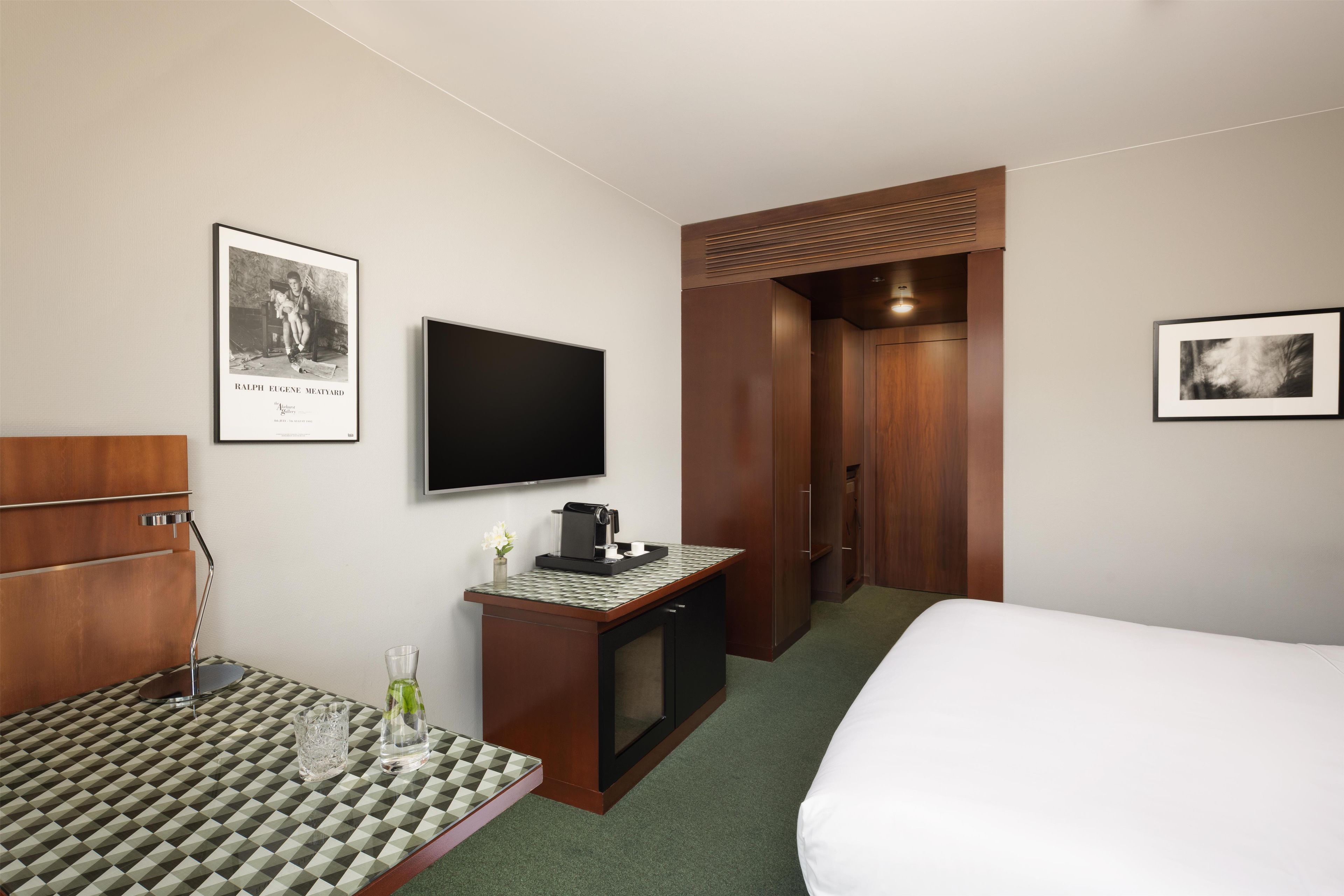 Quarto de hotel com cama, escrivaninha, cafeteira, televisão e guarda-roupa.
