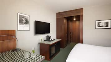 Quarto de hotel com cama, escrivaninha, cafeteira, televisão e guarda-roupa.