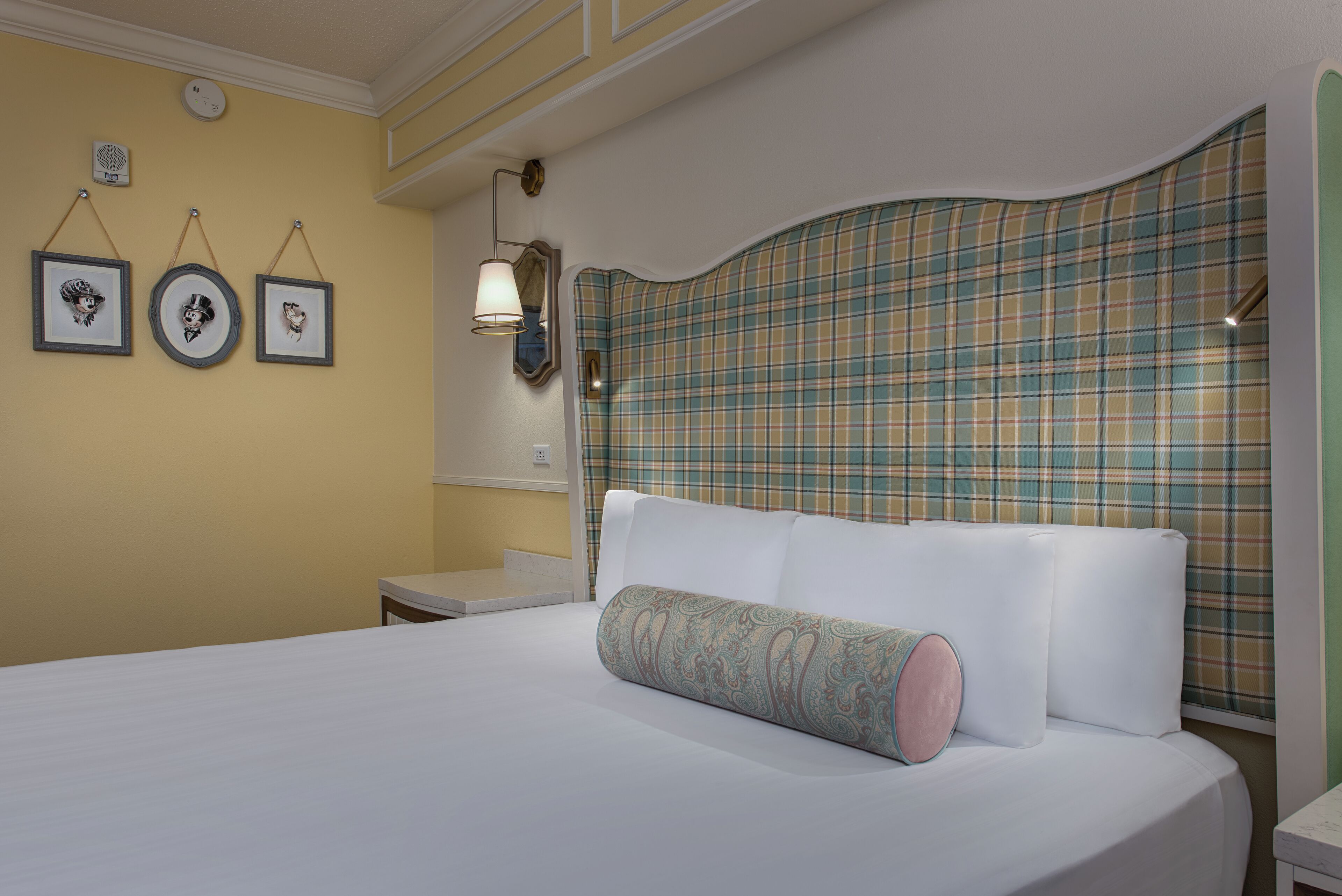 Quarto de hotel com uma cama, cabeceira estampada em xadrez e três quadros na parede.
