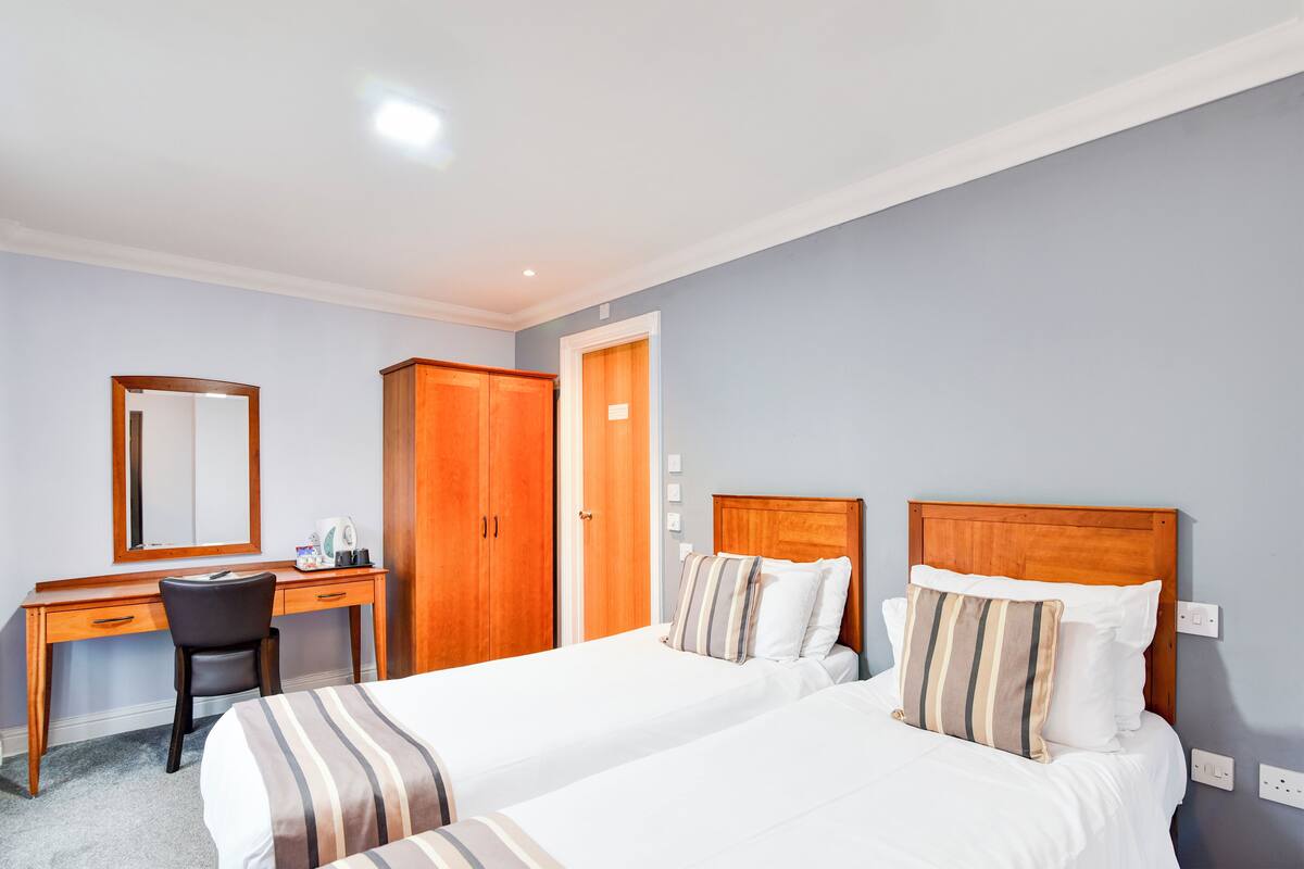 Quarto de hotel com duas camas, uma escrivaninha, uma cadeira e um guarda-roupa.