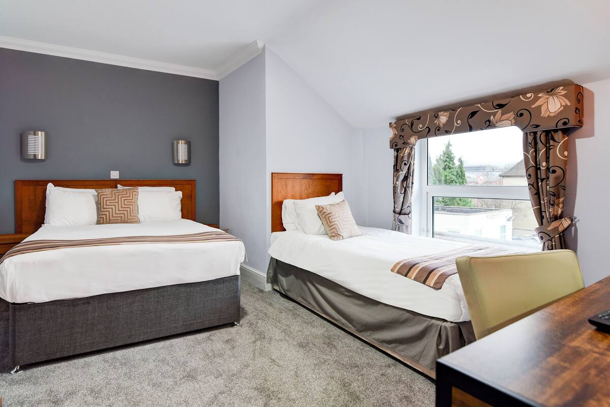 Quarto de hotel com duas camas, uma escrivaninha e uma janela com cortinas.