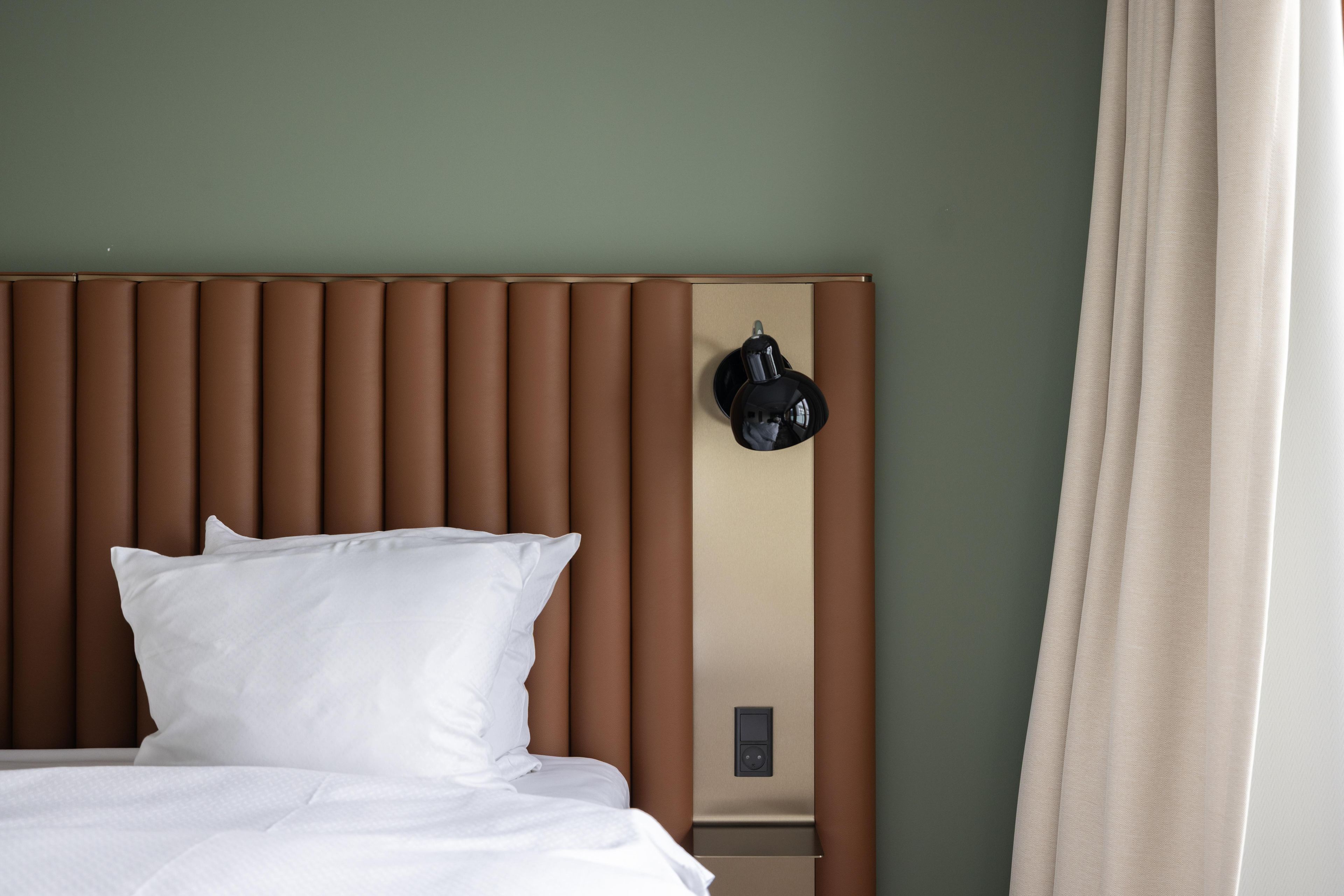 Quarto de hotel com uma cama, cabeceira e luminária fixada na parede.