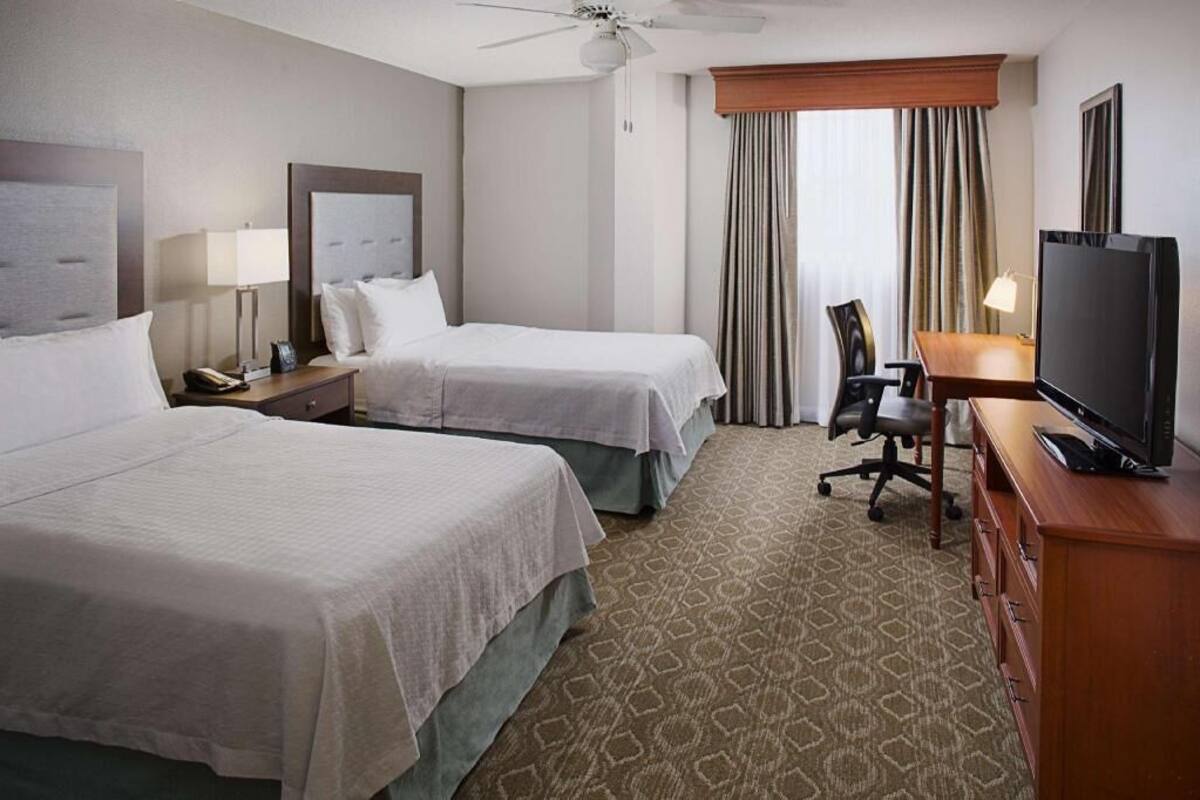 Quarto de hotel com duas camas, televisão, escrivaninha e uma cadeira.