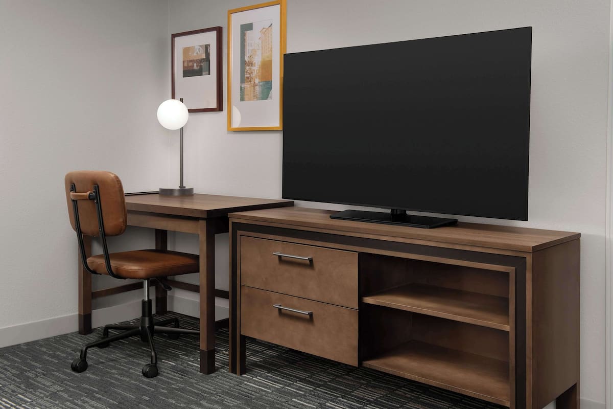 Uma mesa de escritório moderna com uma televisão de tela plana, uma cadeira de couro e um abajur.