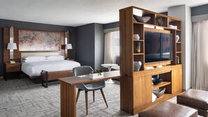 Quarto de hotel moderno com uma cama grande, uma escrivaninha com cadeira, televisão e um móvel de entretenimento em madeira.