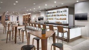 Uma área de bar moderna com várias opções de assento, um bar bem abastecido e uma televisão de tela plana na parede.