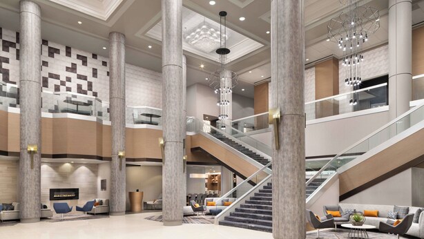 Um hall amplo com pé direito alto, grandes colunas, escadaria e mobiliário moderno.