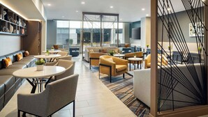Um lobby de hotel moderno com área de sofás, mesas redondas e um painel decorativo.