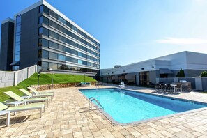 Um edifício moderno com piscina, espreguiçadeiras e área de estar externa.