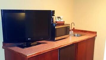 Uma cozinha compacta com televisão integrada, micro-ondas e pia.