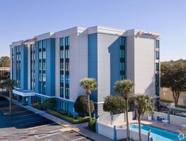 Um hotel moderno com piscina, fachada azul e branca e palmeiras.