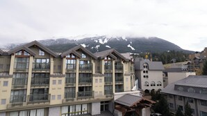 Um hotel com vários andares, varandas e montanhas ao fundo.