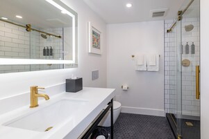 Um banheiro moderno com pia branca, detalhes dourados, box de vidro e piso em azulejo.