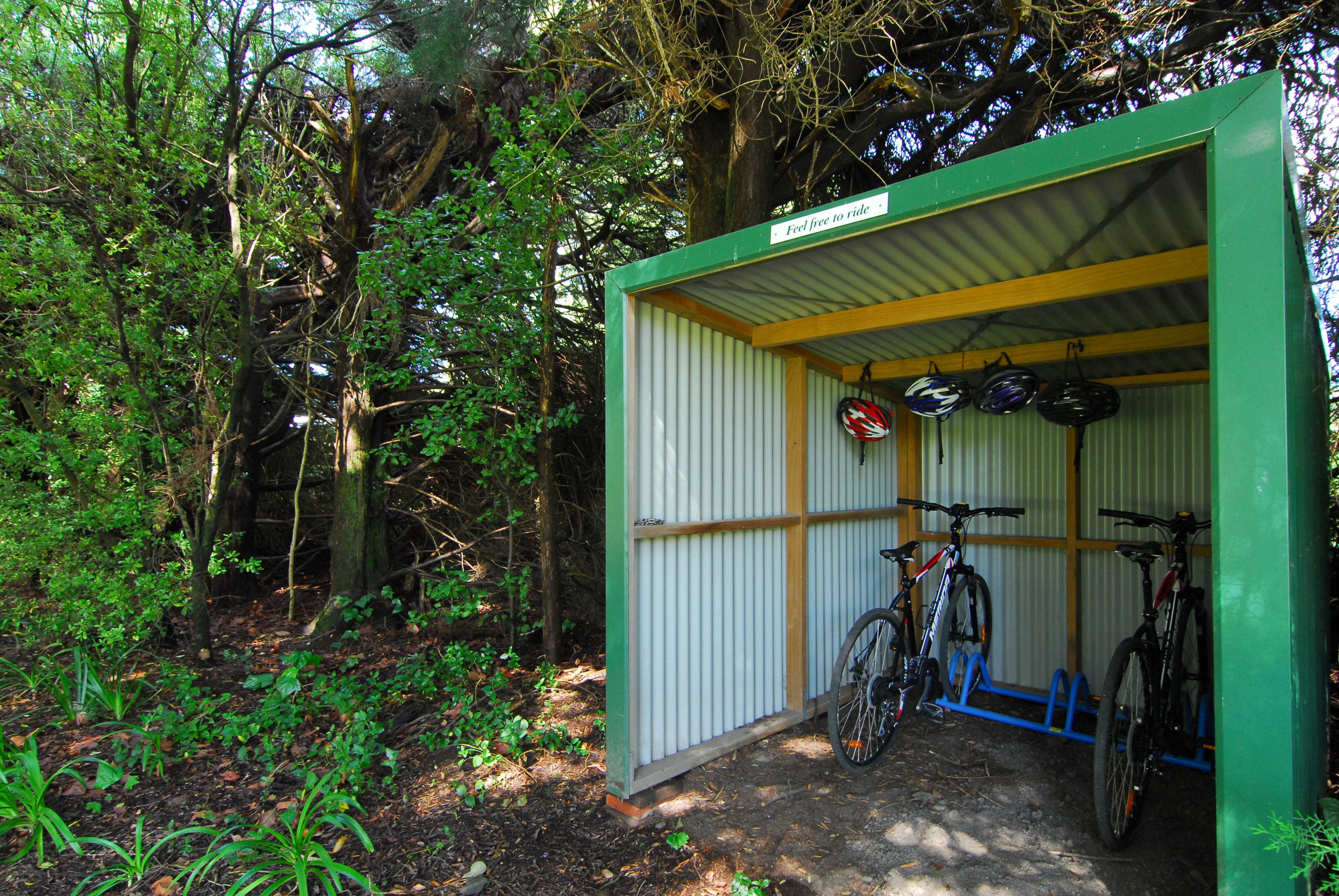 Um pequeno armazém de bicicletas verde e branco, com uma placa que diz 'Sinta-se à vontade para andar'. Lá dentro, há várias bicicletas e capacetes.