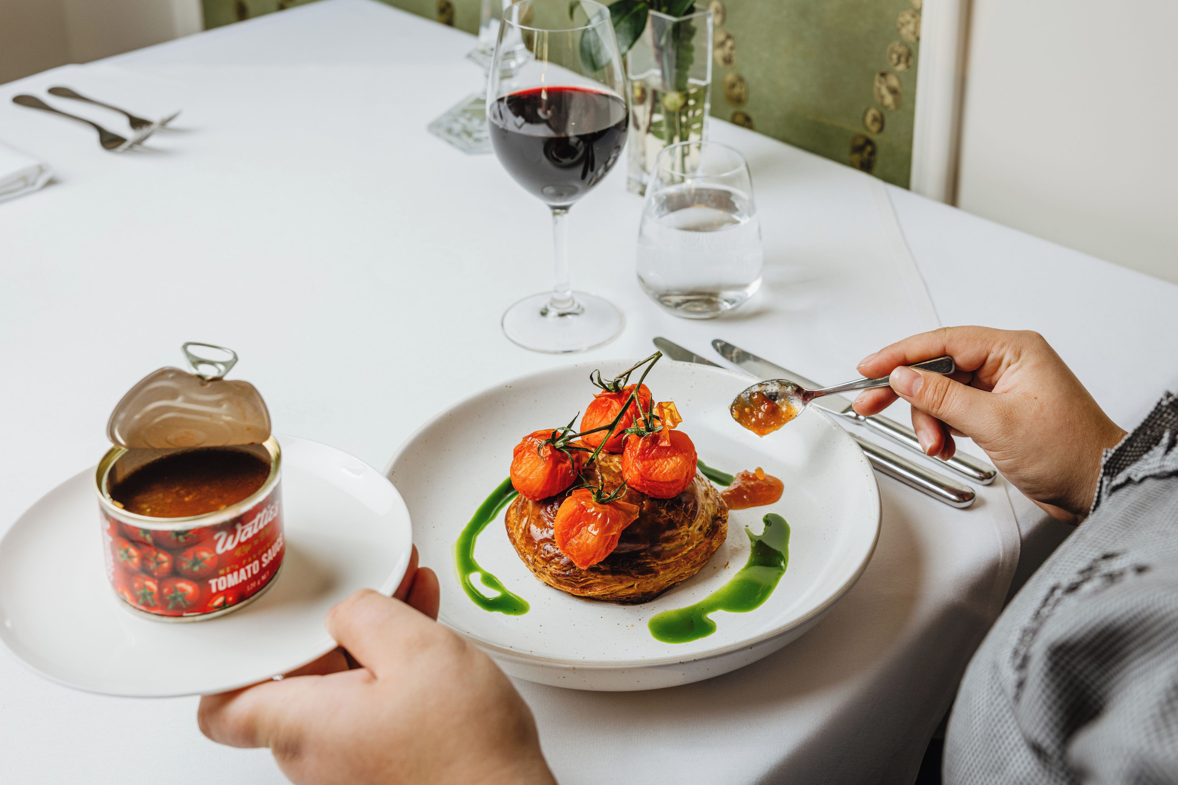 Uma mesa de jantar com um prato de comida, um copo de vinho tinto e uma lata de molho de tomate.