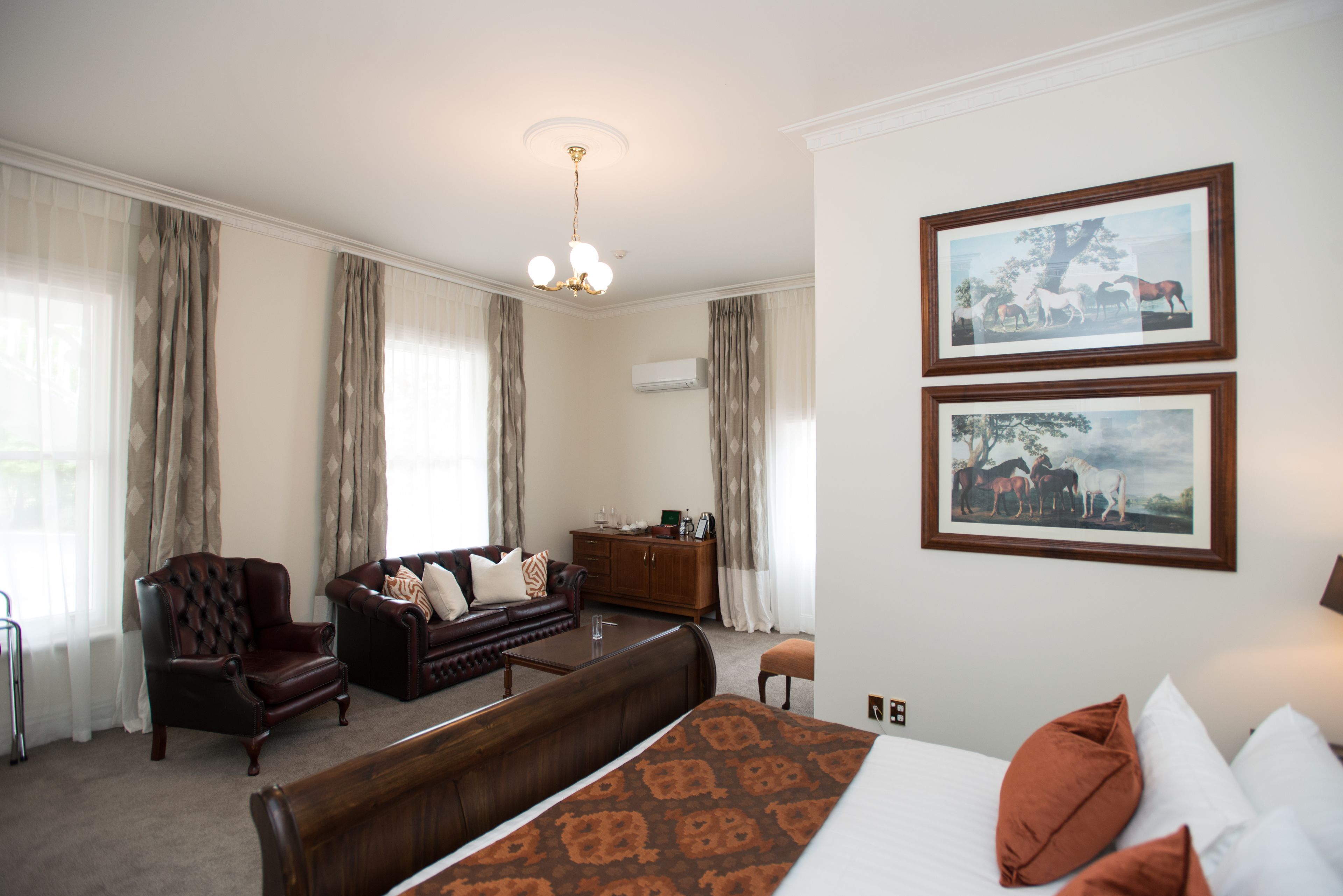 Quarto de hotel com uma cama grande, um sofá, uma cadeira, uma mesa de centro e duas fotografias emolduradas na parede.