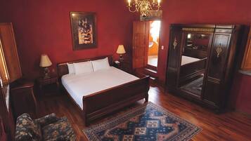 Quarto com uma cama grande, móveis de madeira, um candelabro e uma parede vermelha.