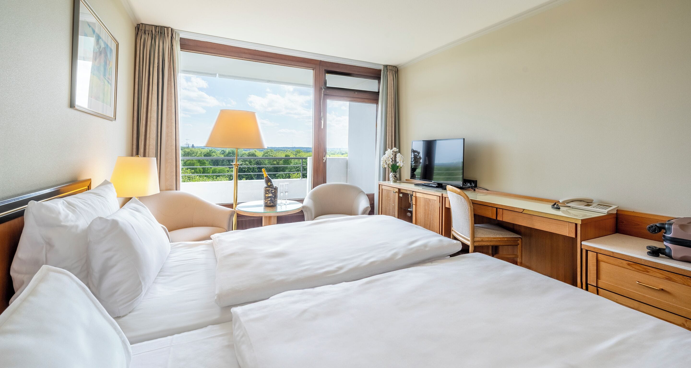 Quarto de hotel com duas camas, uma escrivaninha, uma cadeira, televisão e varanda com vista.