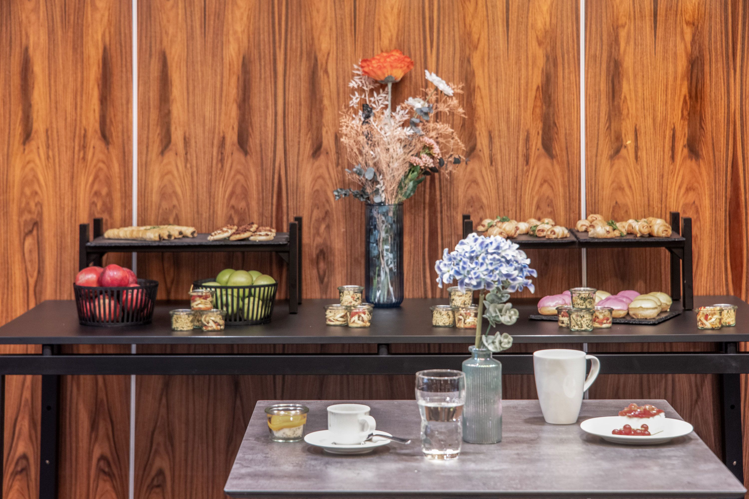Uma mesa de buffet com diversos alimentos e um vaso de flores.