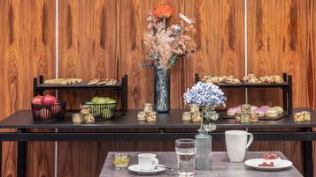 Uma mesa de buffet com diversos alimentos e um vaso de flores.