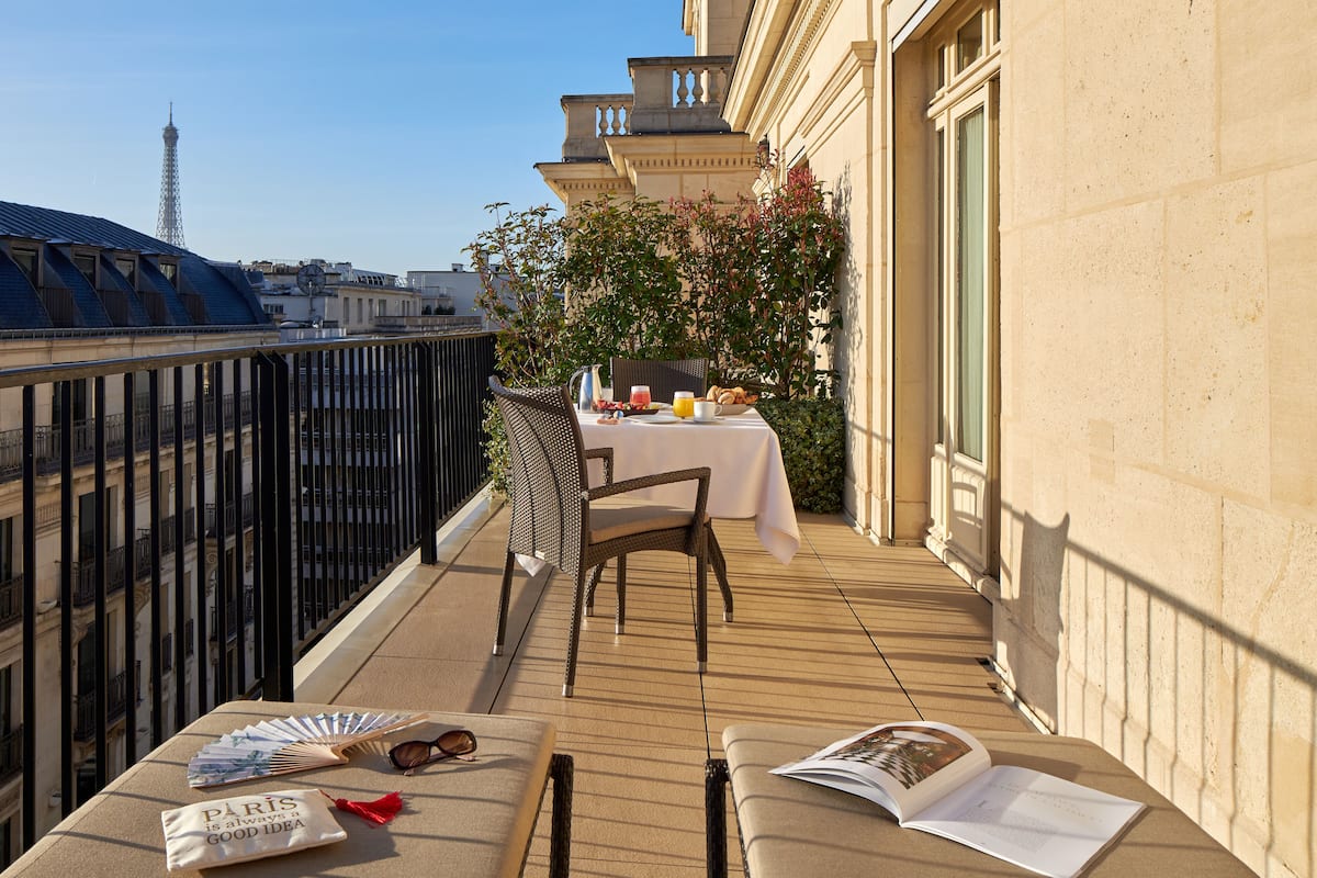 Uma varanda com mesa posta para o café da manhã, uma cadeira de vime e vista para a Torre Eiffel.