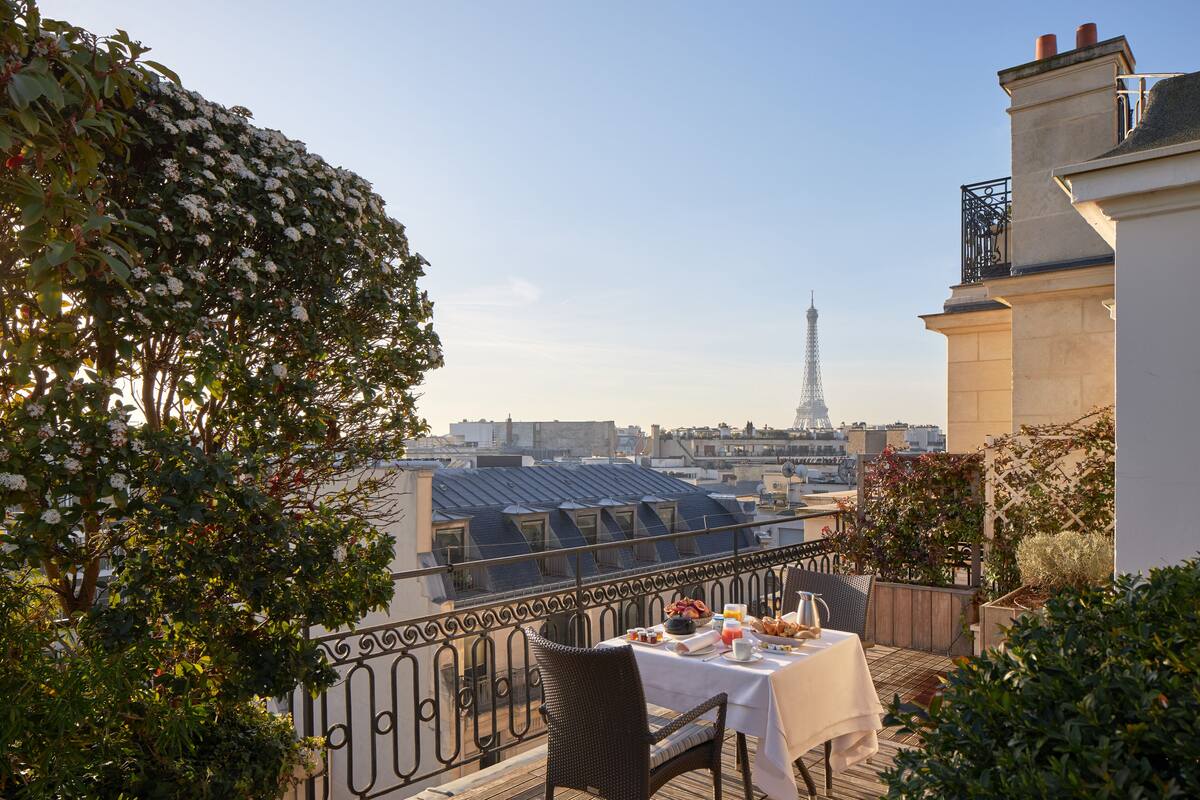 Terraço com mesa posta para o pequeno-almoço, com vista para a cidade e a Torre Eiffel ao longe.