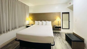 Quarto de hotel com uma cama grande, duas mesas de cabeceira com luminárias, um guarda-roupa e um banco.