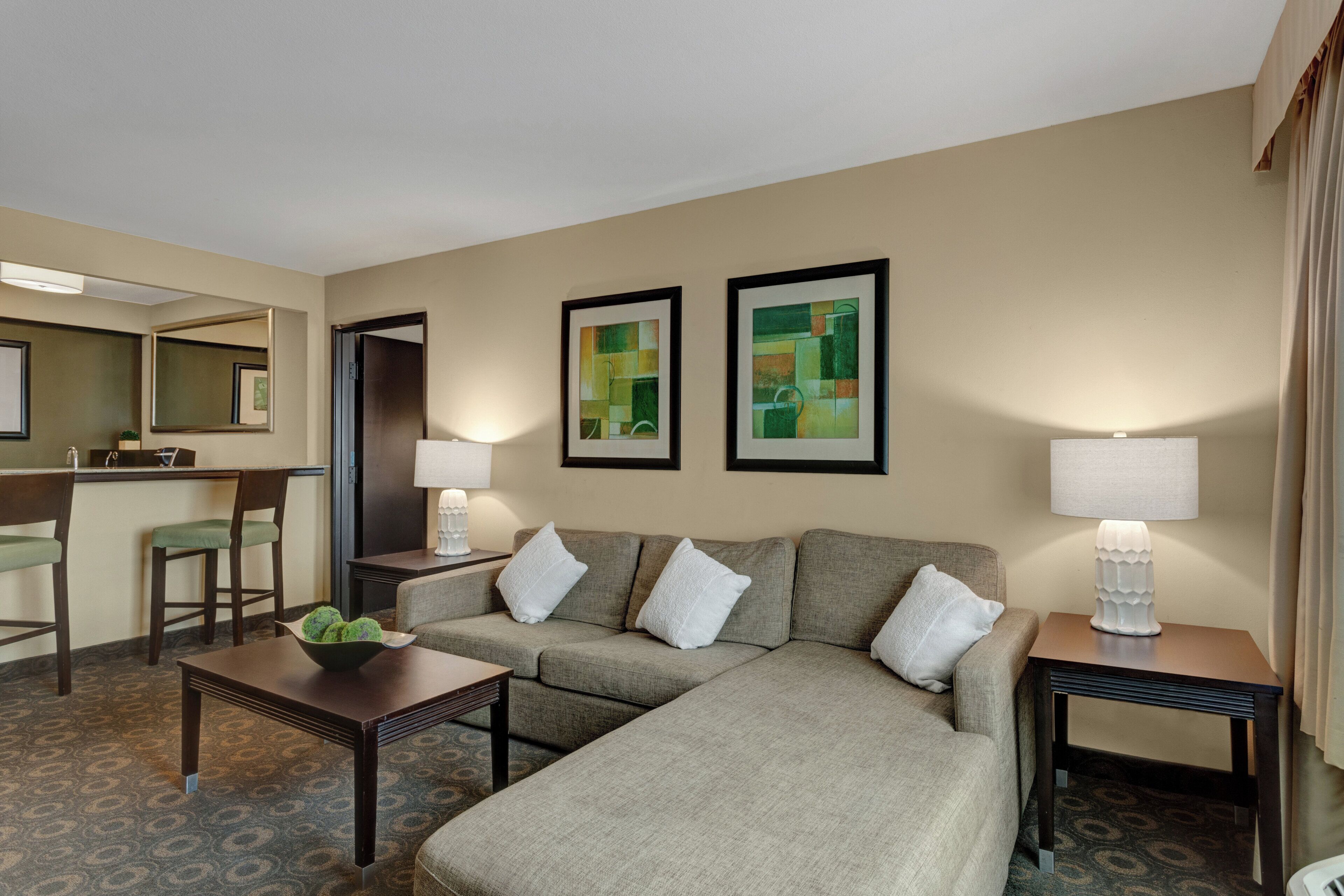 Quarto de hotel com sofá, uma mesinha, candeeiro e uma tigela de frutas.