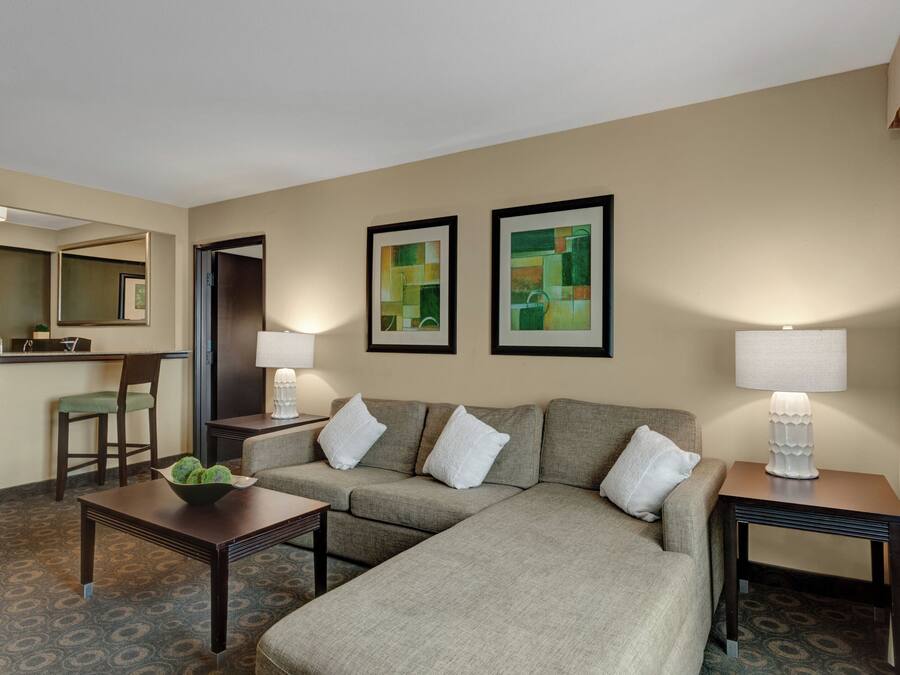 Quarto de hotel com sofá, uma mesinha, candeeiro e uma tigela de frutas.