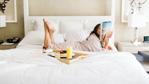 Quarto de hotel com uma cama, um tabuleiro com itens de café da manhã, mesa de cabeceira com telefone e obras de arte nas paredes.