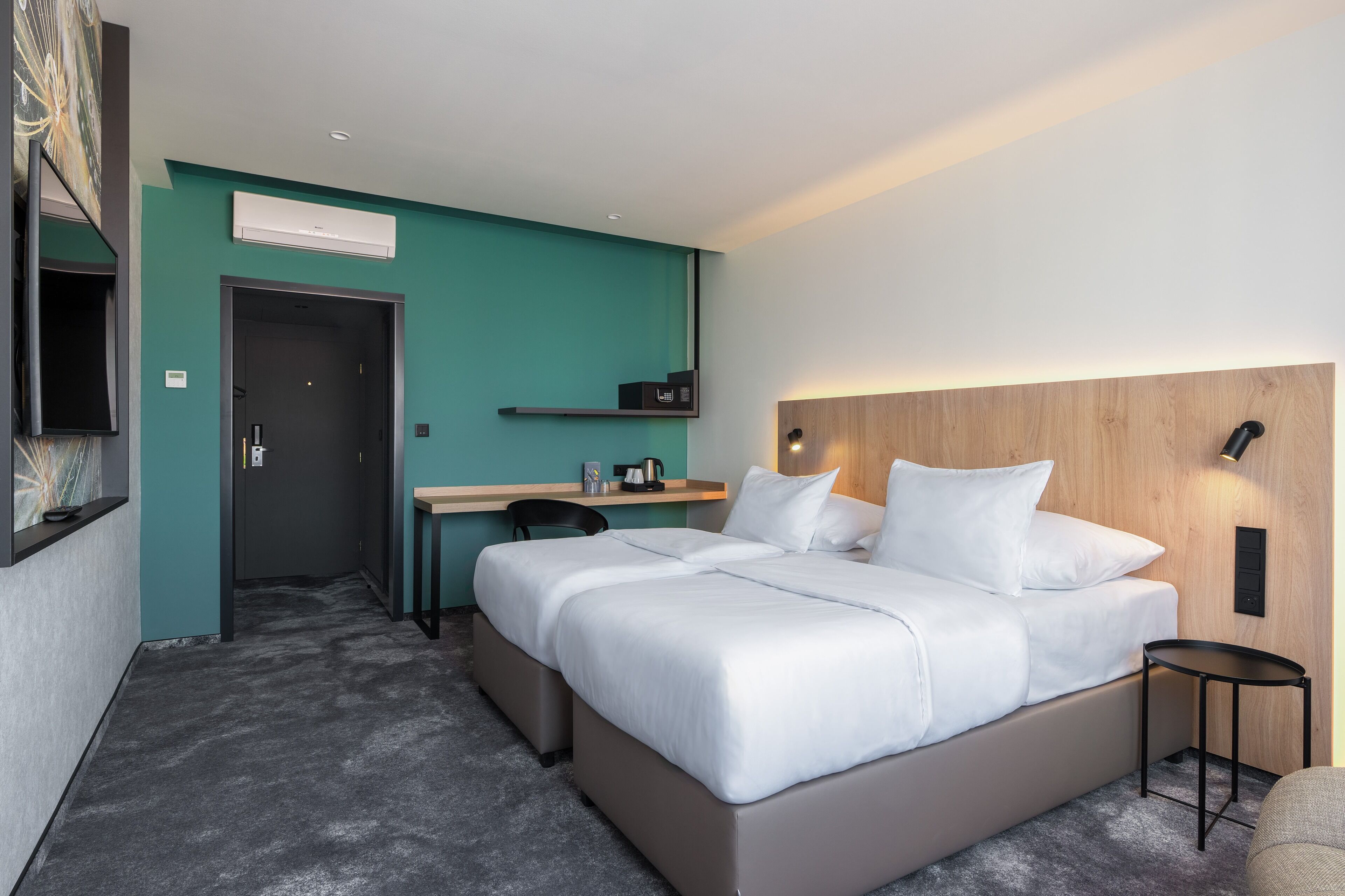 Quarto de hotel moderno com uma cama grande, uma escrivaninha, uma cadeira e uma mesinha.